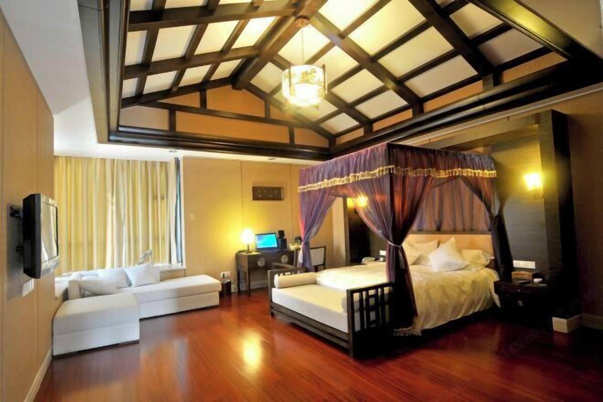 Quarto com cama de dossel, sofá, televisão e escrivaninha.