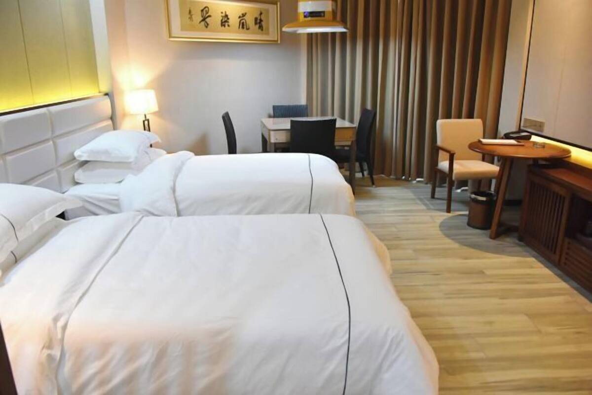 Quarto de hotel com duas camas, uma escrivaninha, uma cadeira e uma pequena mesa.
