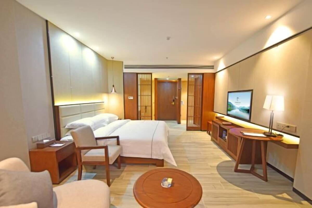 Quarto de hotel com cama, escrivaninha, televisão e área de estar.