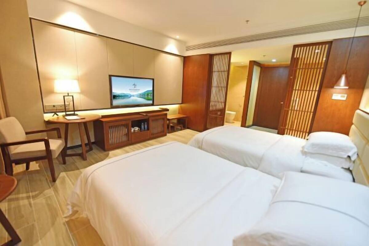 Quarto de hotel com duas camas, televisão, escrivaninha e uma cadeira.