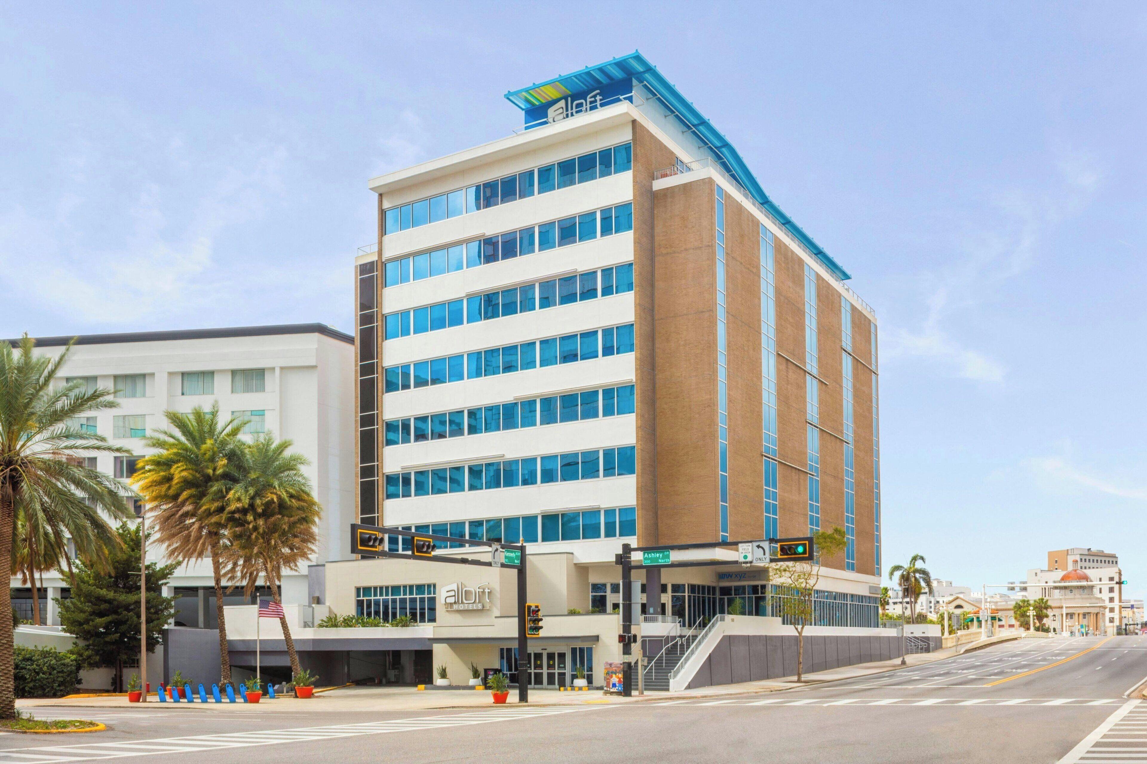 Um hotel moderno com uma placa chamativa da marca 'aloft', vários andares e um telhado plano.
