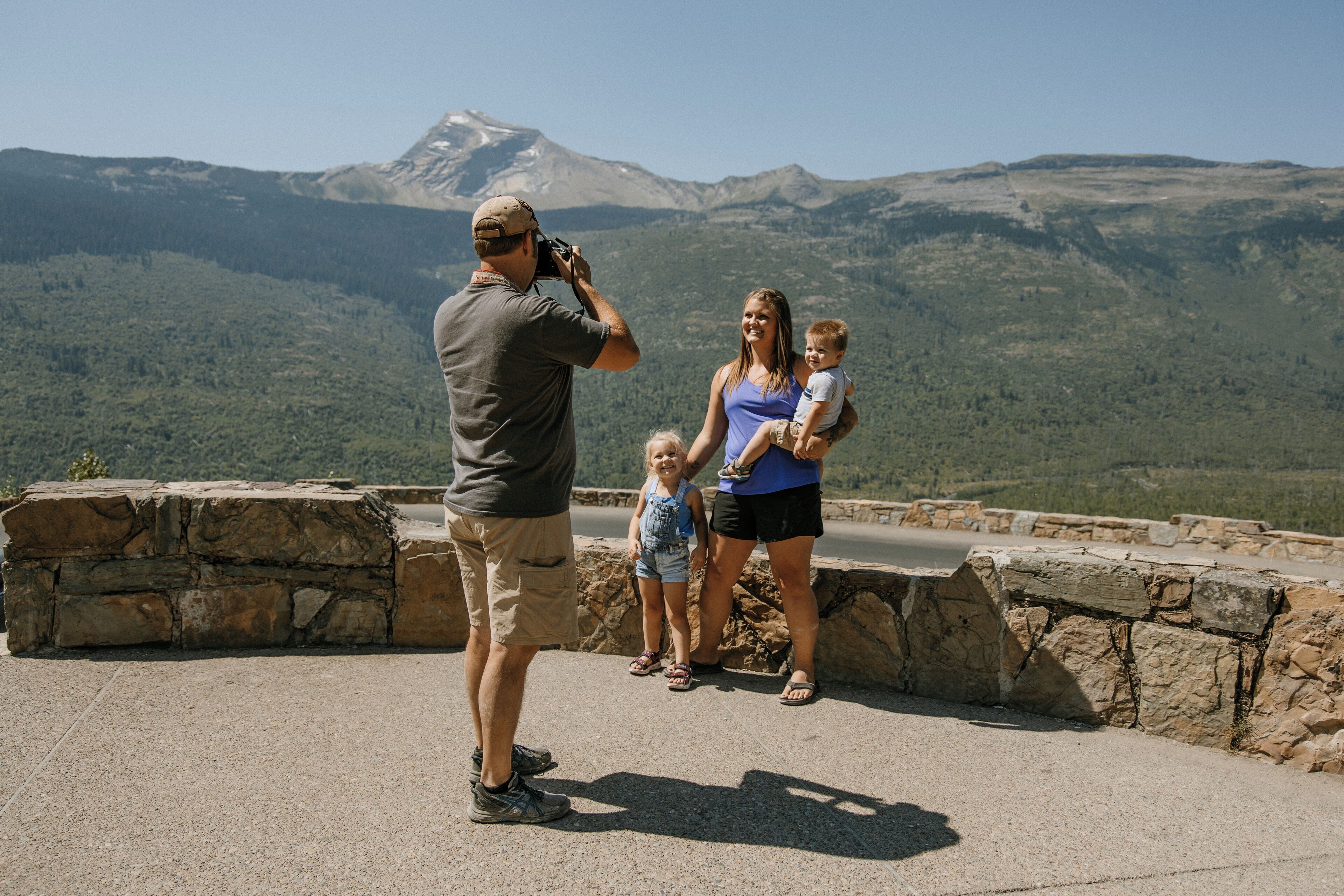 Uma família de quatro pessoas em um mirante com uma paisagem deslumbrante, com um fotógrafo registrando o momento.