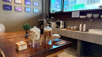 Cozinha de hotel com mesa de madeira, um vaso pequeno com planta, um pote de vidro com biscoitos e um aviso solicitando aos hóspedes que limpem após o uso.
