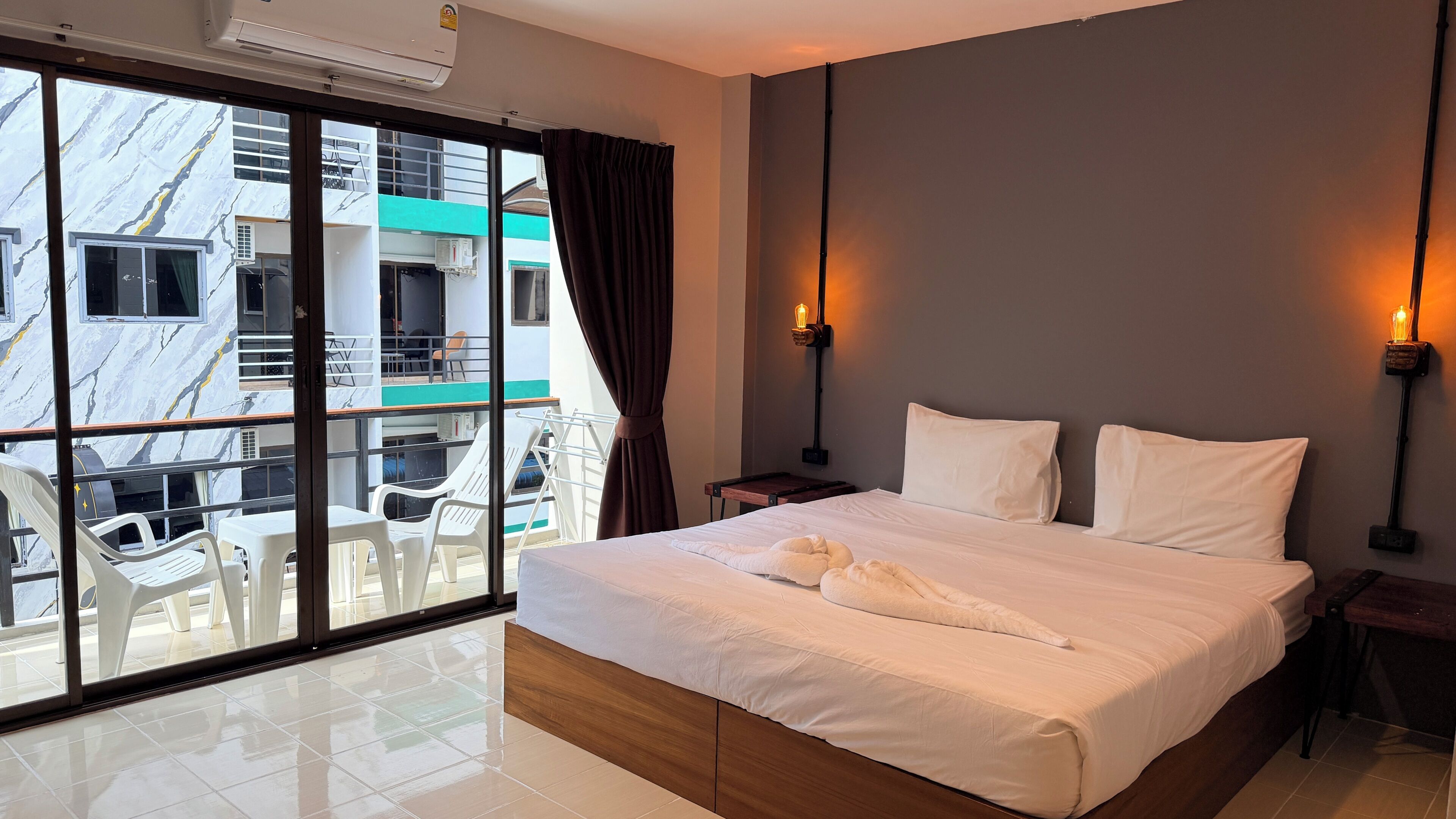 Quarto de hotel com uma cama grande, duas luminárias laterais, vista para a varanda externa e uma janela com cortinas.