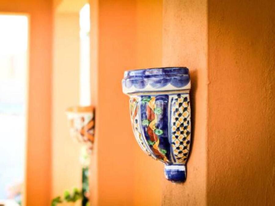 Uma peça decorativa de cerâmica na parede, com padrão azul e amarelo, sobre um fundo laranja quente.