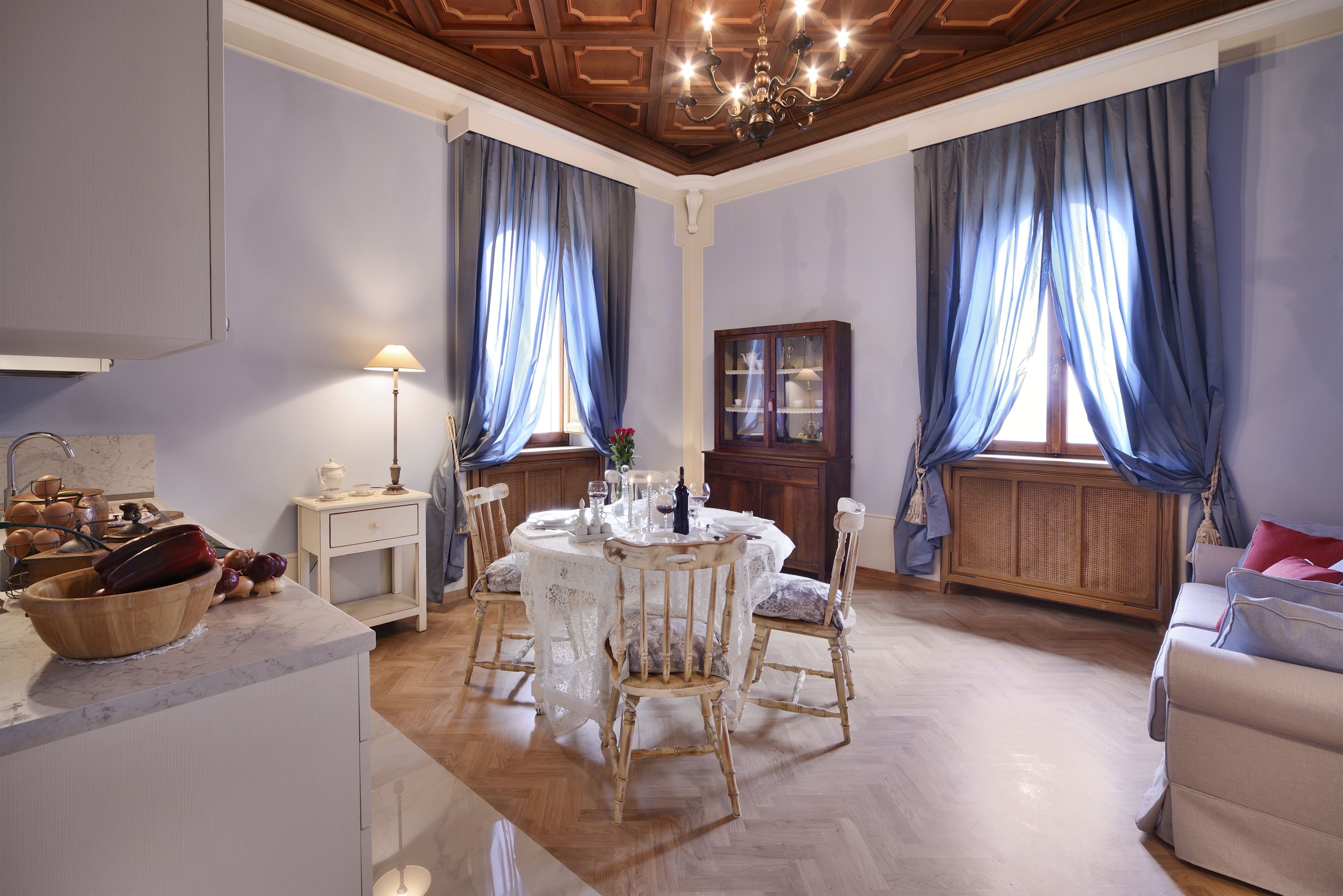 Uma área de refeições com uma mesa redonda, cadeiras, um lustre e um aparador com portas de vidro.