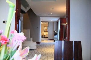 Um corredor de hotel com carpete estampado, um sofá branco e uma área de refeições ao fundo.