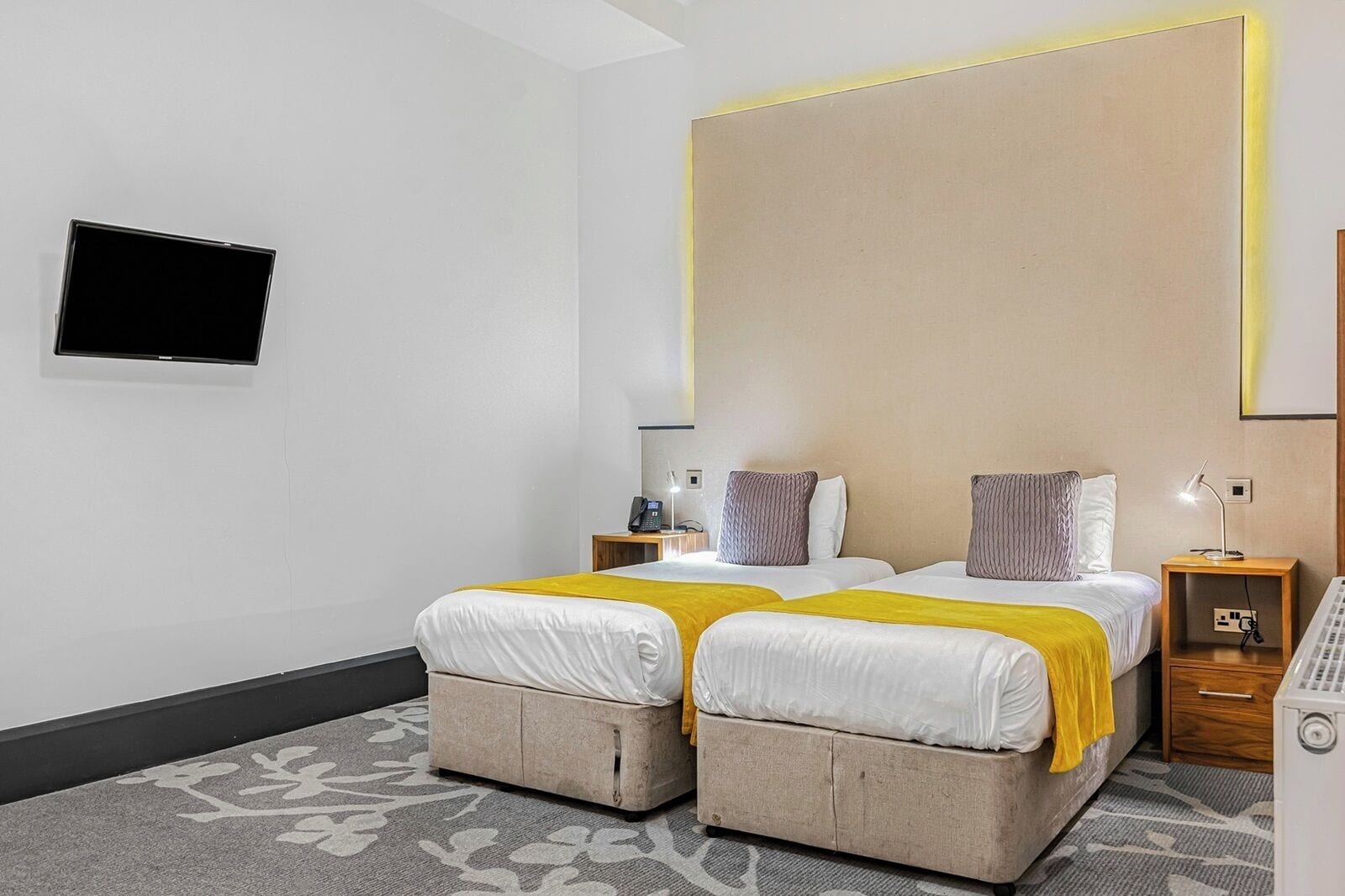 Quarto de hotel com duas camas, televisão de tela plana, mesas de cabeceira com abajures e piso coberto por carpete.