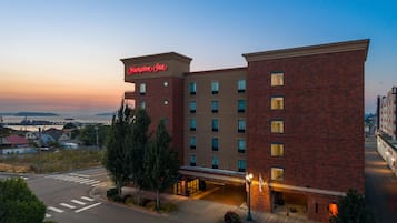 Um hotel Hampton Inn com fachada de tijolos, vários andares e estacionamento.