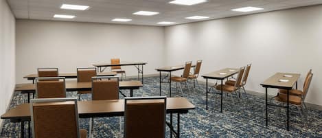 Sala de conferência com mesas, cadeiras, piso coberto por carpete e iluminação no teto.