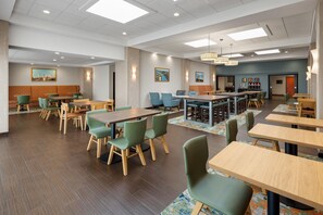 Uma sala de jantar ampla com várias mesas e cadeiras, diversas opções de assento e um design moderno no teto.