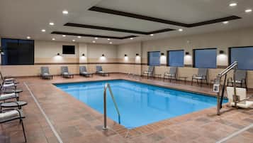 Área de piscina de hotel com piscina retangular, espreguiçadeiras e piso cerâmico.