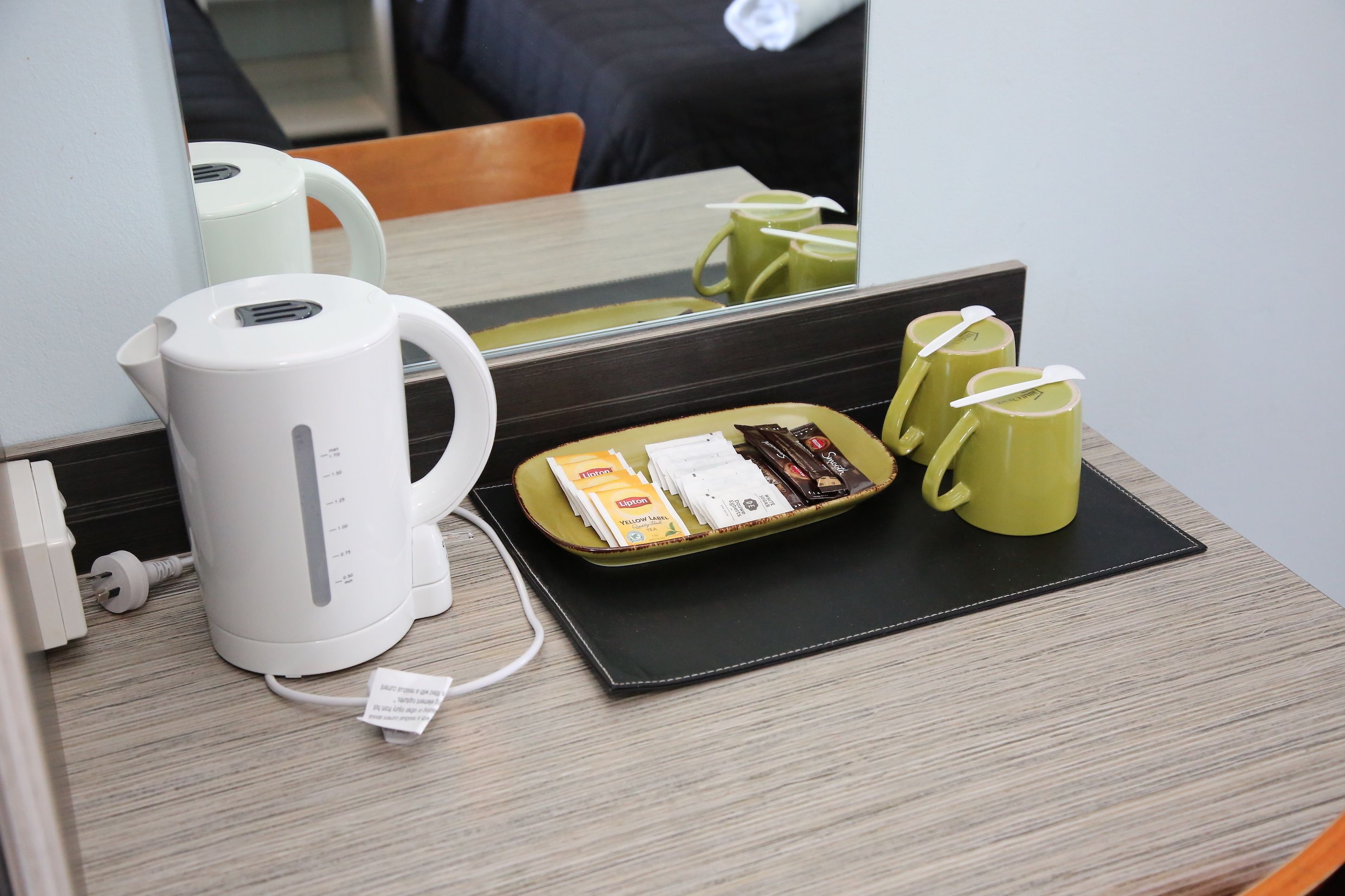Quarto de hotel com máquina de café, duas canecas verdes e um tabuleiro com saquinhos de chá e aperitivos.