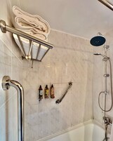 Uma casa de banho moderna com chuveiro de entrada direta, porta de vidro para a toalheira e artigos de higiene pessoal na parede.