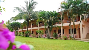 Um hotel com vários andares, varandas e muita vegetação, incluindo palmeiras e jardins bem cuidados.