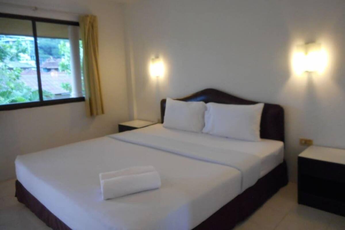Quarto de hotel com uma cama grande, duas mesas de cabeceira, uma janela com cortinas e luminárias na parede.