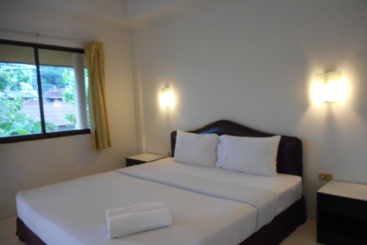 Quarto de hotel com cama grande, duas mesas de cabeceira e uma janela com cortinas.