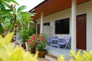 Área externa coberta com plantas em vasos, teto de madeira e uma porta com o número 110.