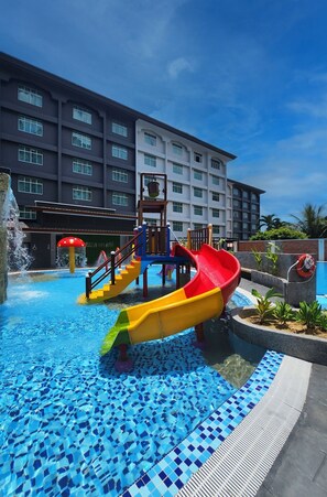 Parque aquático com escorregadores e piscina, cercado por um edifício com várias janelas.