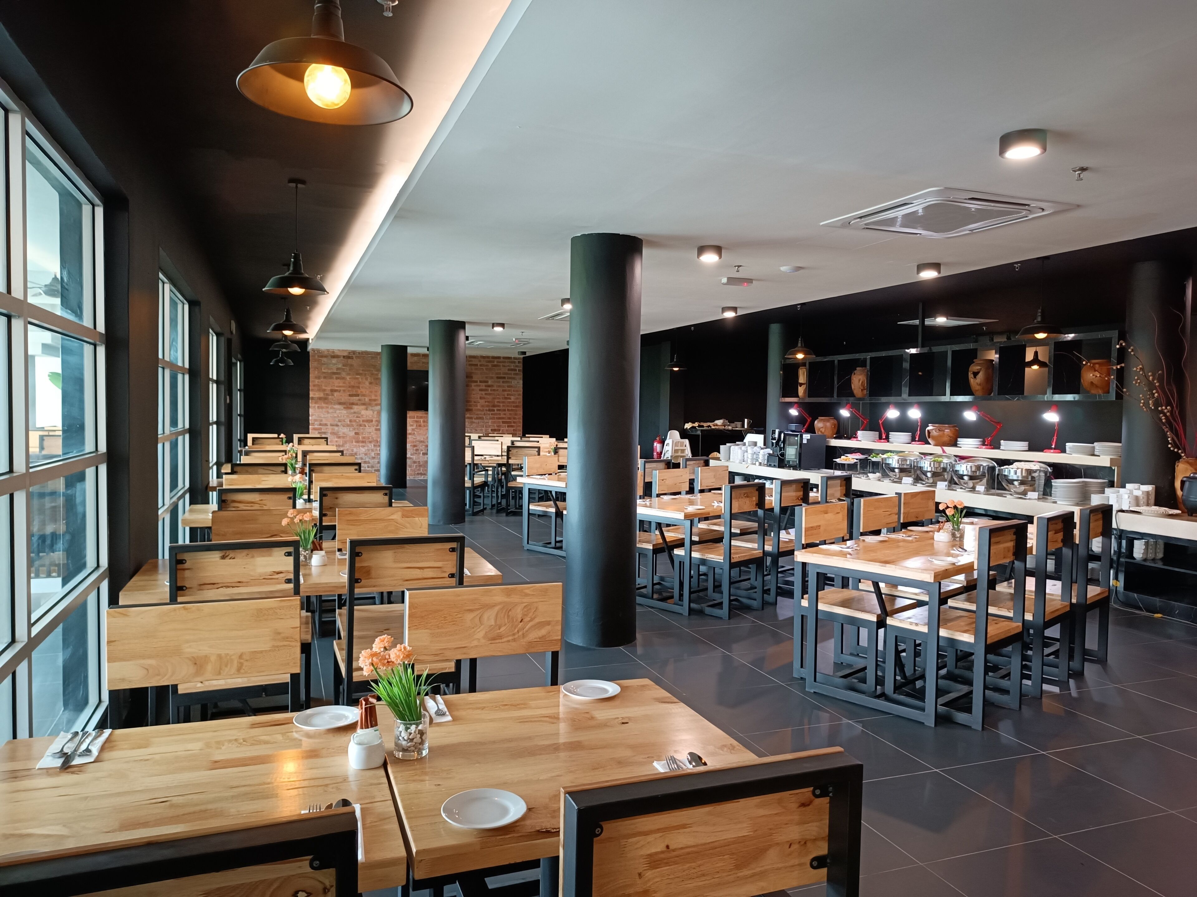 Restaurante moderno com mesas e cadeiras de madeira, grandes janelas e uma parede de tijolos.