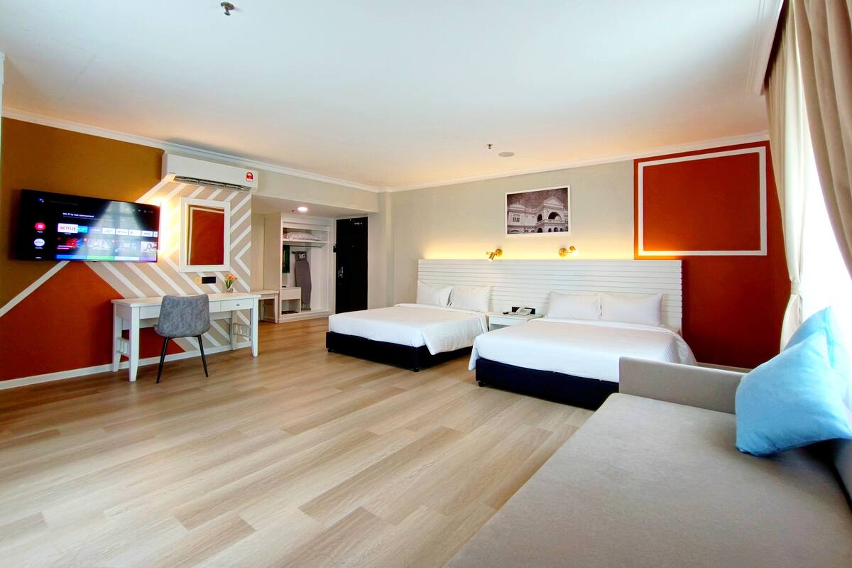 Quarto de hotel com duas camas, uma escrivaninha, uma televisão e um guarda-roupa.