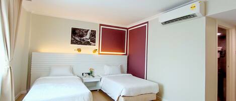 Quarto de hotel com duas camas, uma mesinha de cabeceira com abajur, um quadro na parede e um ar condicionado.