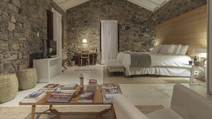 Um quarto aconchegante com parede de pedra, cama com roupa de cama branca, cabeceira de madeira, mesa de cabeceira com abajur e TV em um suporte.