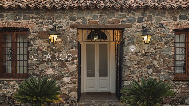 Edifício de pedra com uma placa que diz 'CHARCO' e duas plantas em vasos na frente.