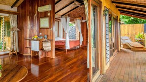 Interior de madeira com uma cama, uma mesa com abajur e vista para o exterior.