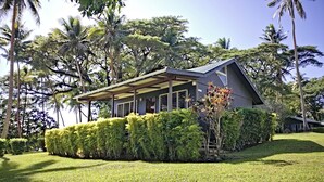 Uma casa com varanda coberta, cercada por sebes bem cuidadas e palmeiras.