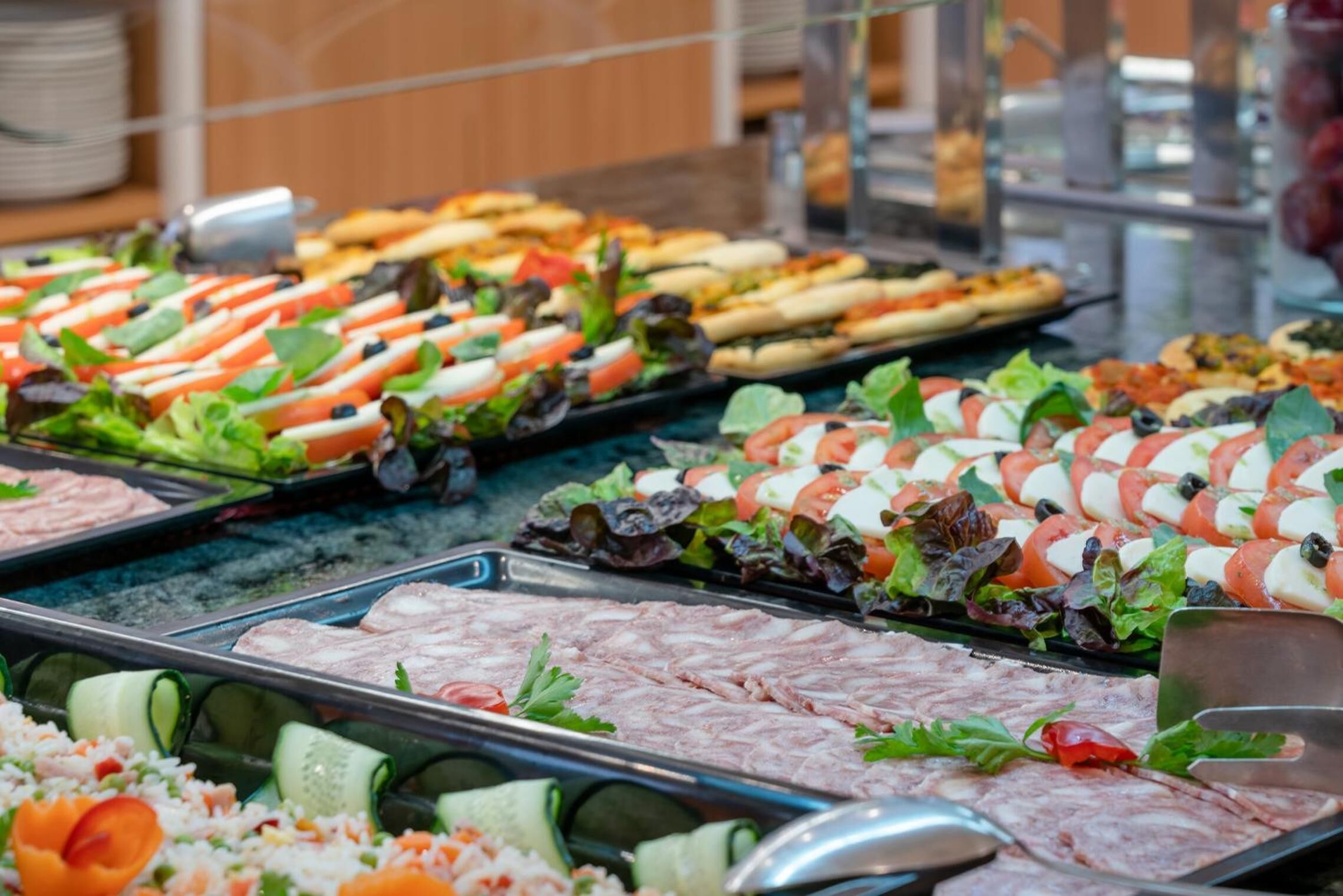 Buffet com diversas opções de comida, incluindo saladas, sanduíches e frios.