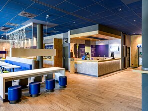 Um saguão moderno de hotel com balcão de recepção, área de estar e bar.