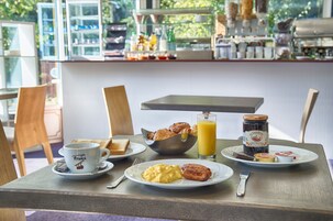 Uma mesa de café da manhã com croissants, ovos mexidos, torradas, uma xícara de café, um copo de suco de laranja e um pote de geleia.
