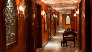 Um corredor com portas de madeira, janelas em arco e luminárias fixadas na parede.