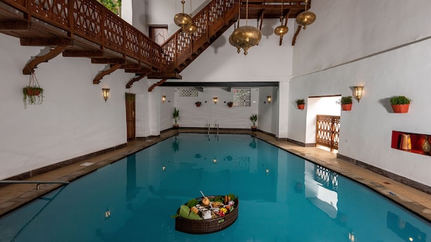 Uma piscina interna com um barco de madeira repleto de comida e bebidas, cercada por paredes brancas e corrimãos de madeira.