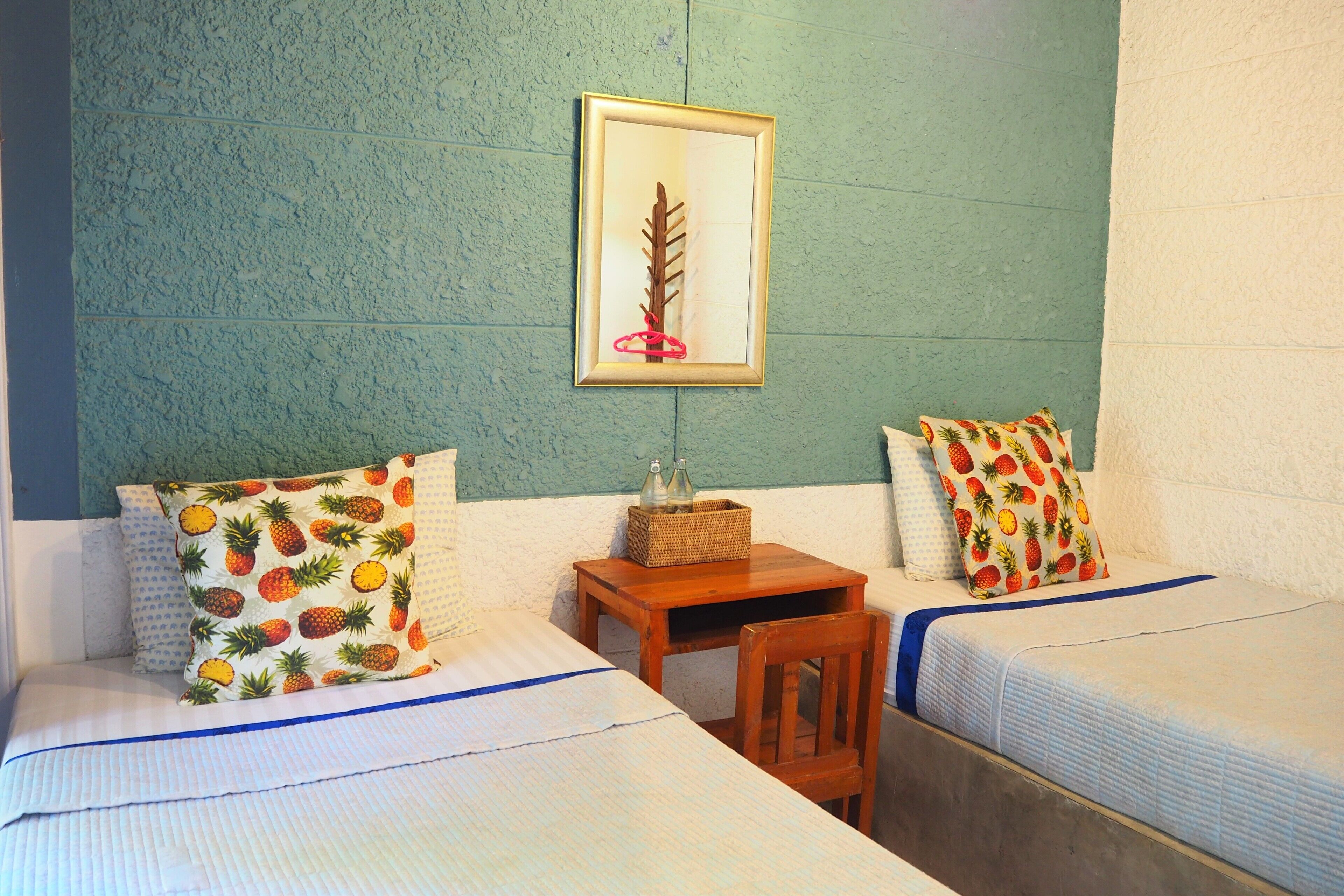 Quarto com duas camas, cada uma com almofada estampada com abacaxi e um quadro na parede.