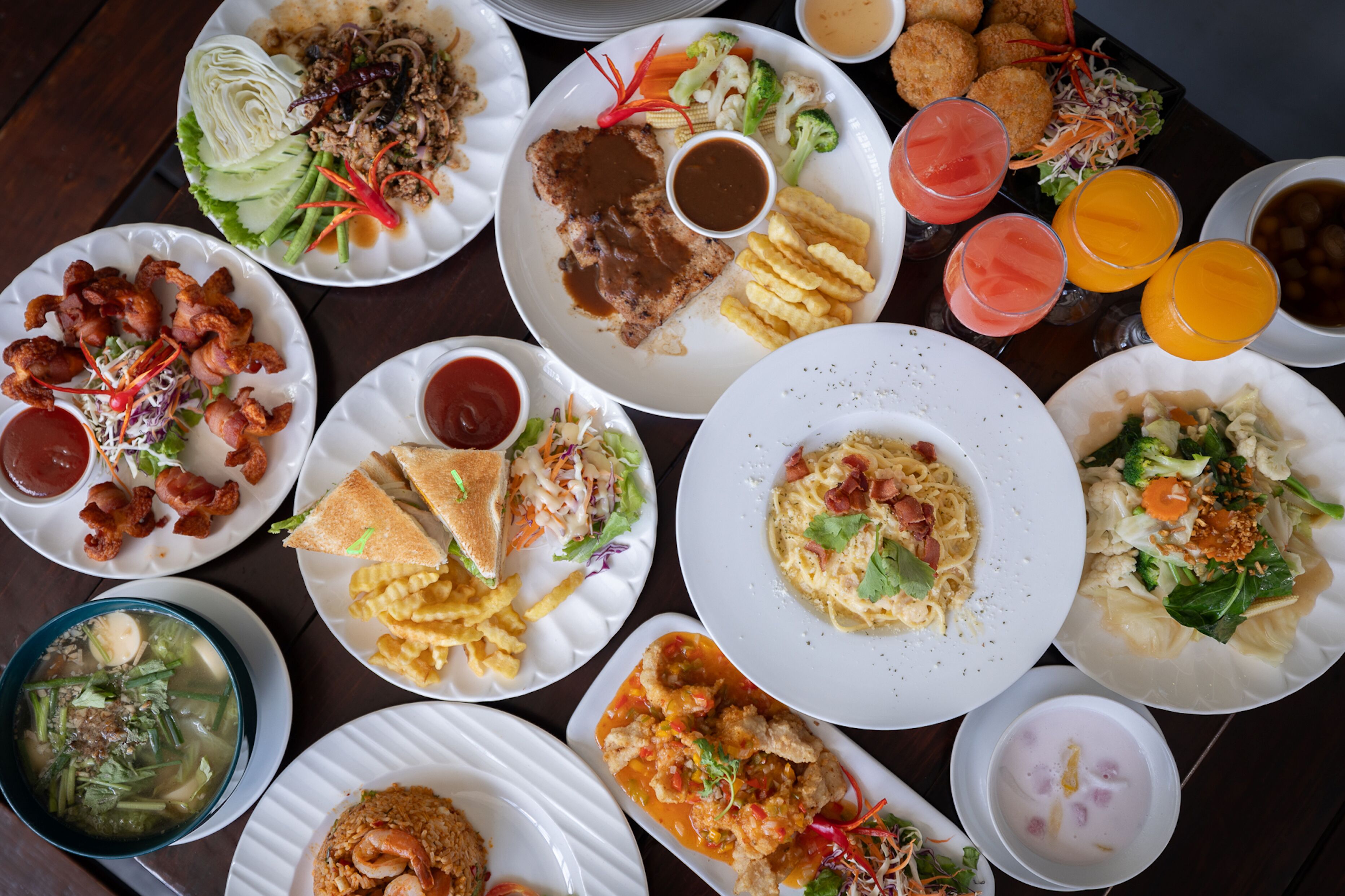 Diversos pratos, incluindo frituras, saladas e bebidas, sobre uma mesa.