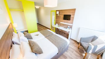 Quarto de hotel moderno com cama, escrivaninha, cadeira e televisão.