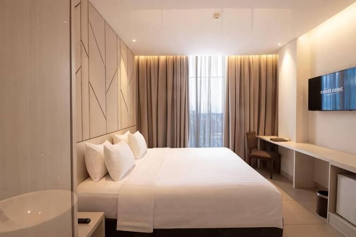 Quarto de hotel moderno com uma cama grande, uma escrivaninha, uma cadeira, uma TV e vista para a cidade.