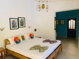 Quarto com cama de madeira, roupa de cama branca, almofada colorida e porta com design geométrico.