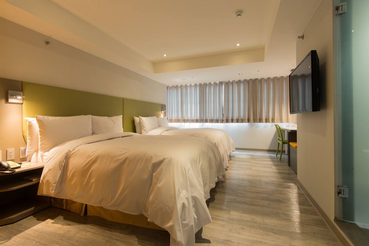 Quarto de hotel com duas camas, uma escrivaninha e uma televisão.