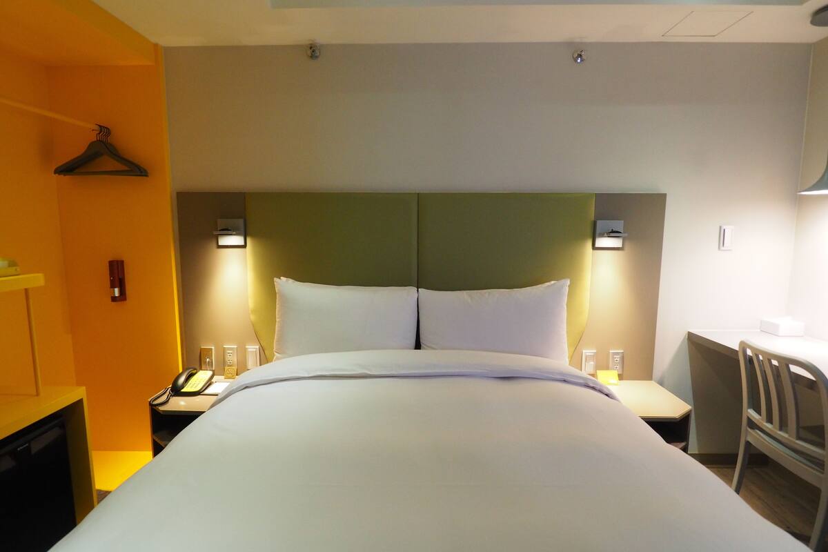 Quarto de hotel com uma cama grande, mesas de cabeceira, uma escrivaninha e uma cadeira.