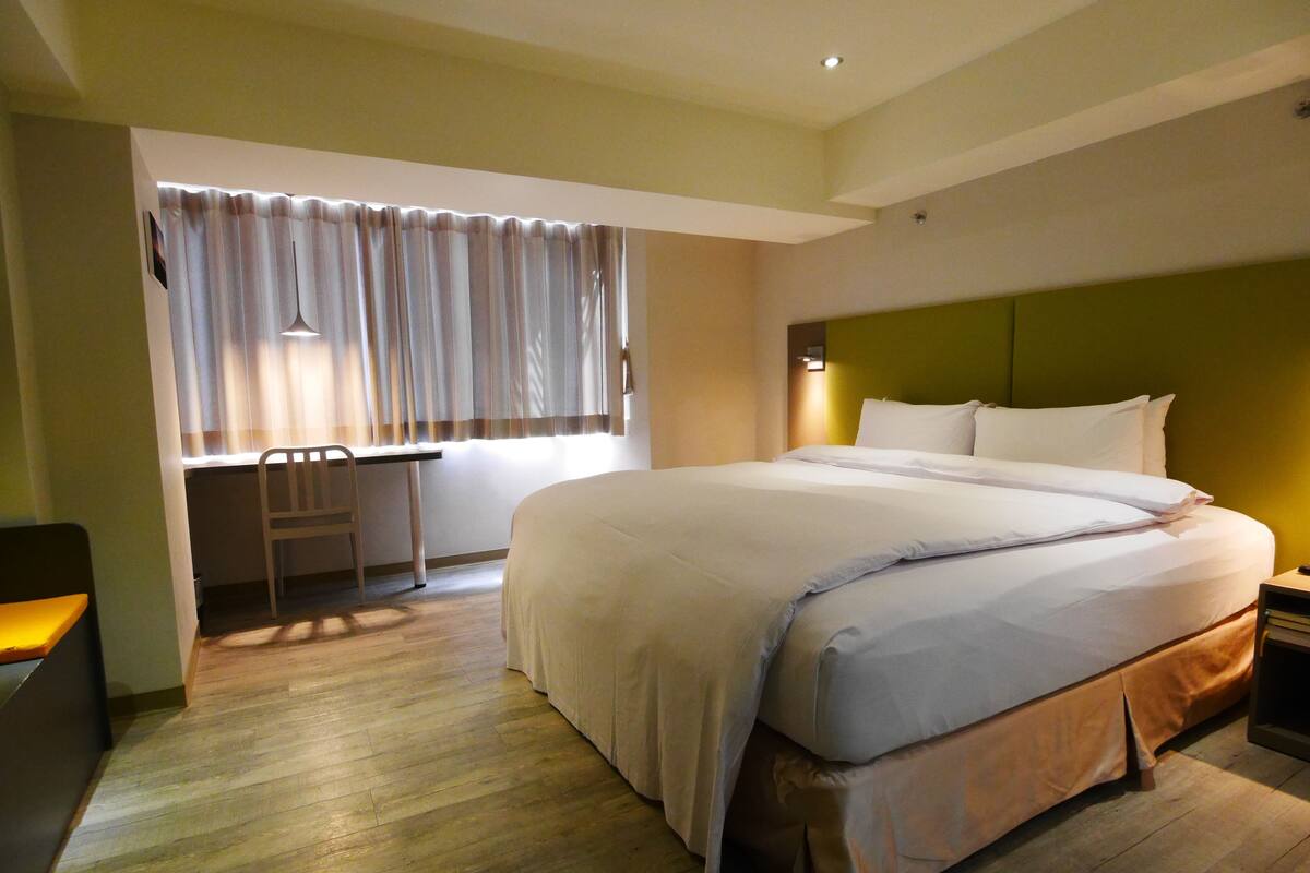 Quarto de hotel com uma cama grande, uma escrivaninha e uma cadeira.