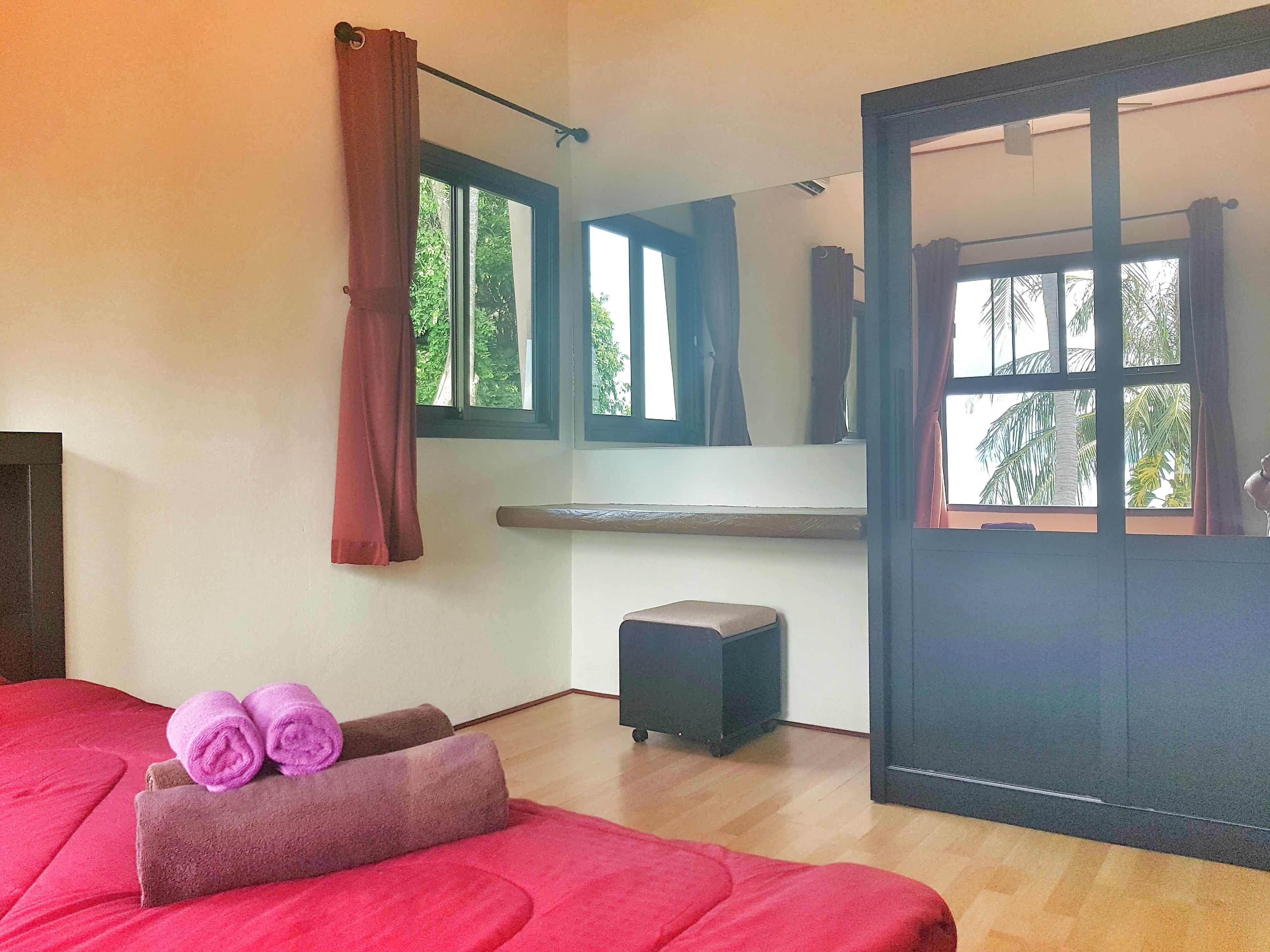 Quarto com uma cama, um banquinho, um espelho e uma janela com cortinas.