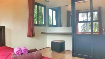 Quarto com uma cama, um banquinho, um espelho e uma janela com cortinas.