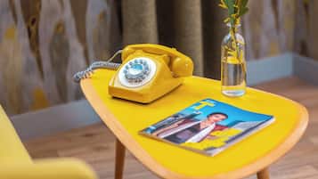 Um telefone amarelo sobre uma mesa de madeira, com uma revista e um vaso com flores amarelas.
