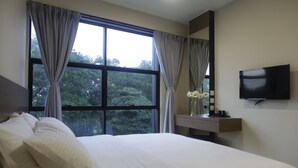 Quarto de hotel com uma cama grande, televisão de tela plana fixada na parede e uma janela com cortinas.