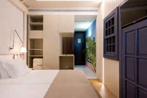 Quarto de hotel com cama, guarda-roupa, escrivaninha e uma pequena cozinha.
