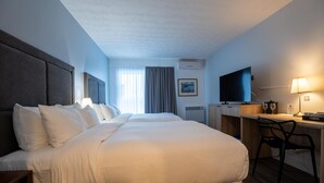 Quarto de hotel com duas camas, uma escrivaninha, uma cadeira, uma televisão e um abajur.