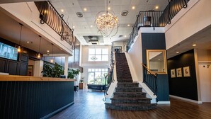 Um hall espaçoso com uma escadaria imponente, um balcão de recepção e um lustre grande.